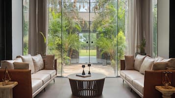 Uma sala de estar ampla com uma grande porta de vidro que dá para um jardim, dois sofás de couro, uma mesa de centro redonda e decoração minimalista.