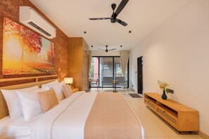 Quarto de hotel com uma cama grande, ventoinha no teto, pintura de uma floresta, escrivaninha com cadeira e vista para o exterior.
