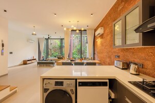 Cozinha moderna com máquina de lavar e secar embutidas, área de jantar com vista para o jardim e uma janela grande com cortinas.