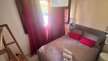 Quarto com cama, escada de madeira, luminária pendente e janela com cortinas.