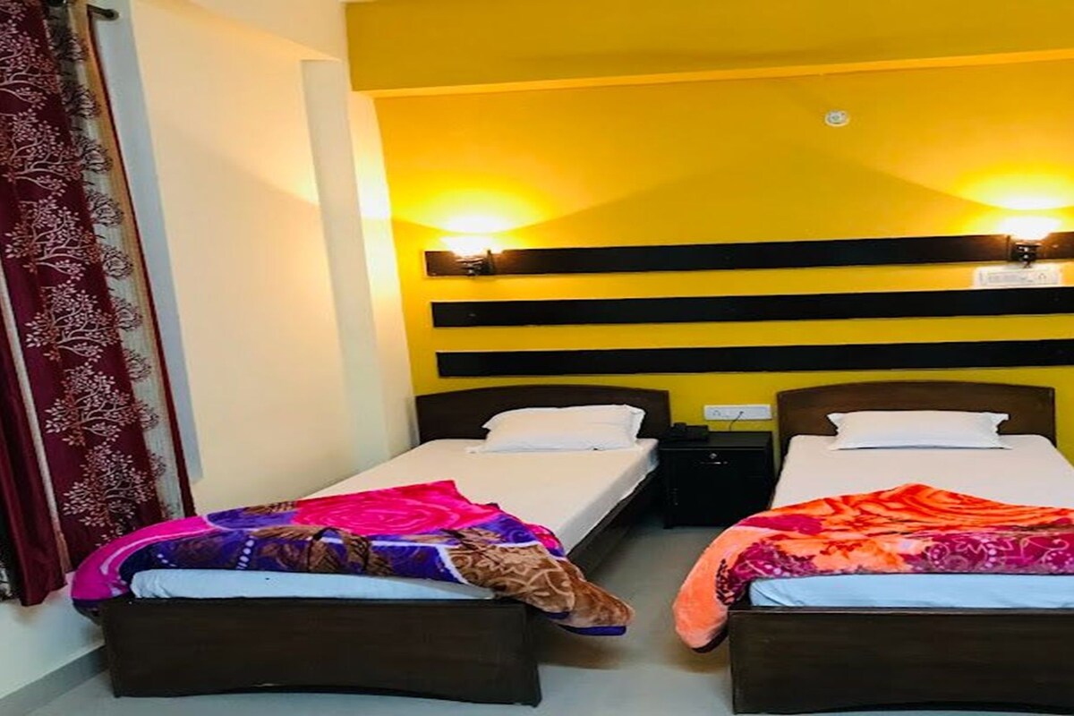 Quarto de hotel com duas camas de solteiro, uma parede de destaque amarela e uma porta preta.