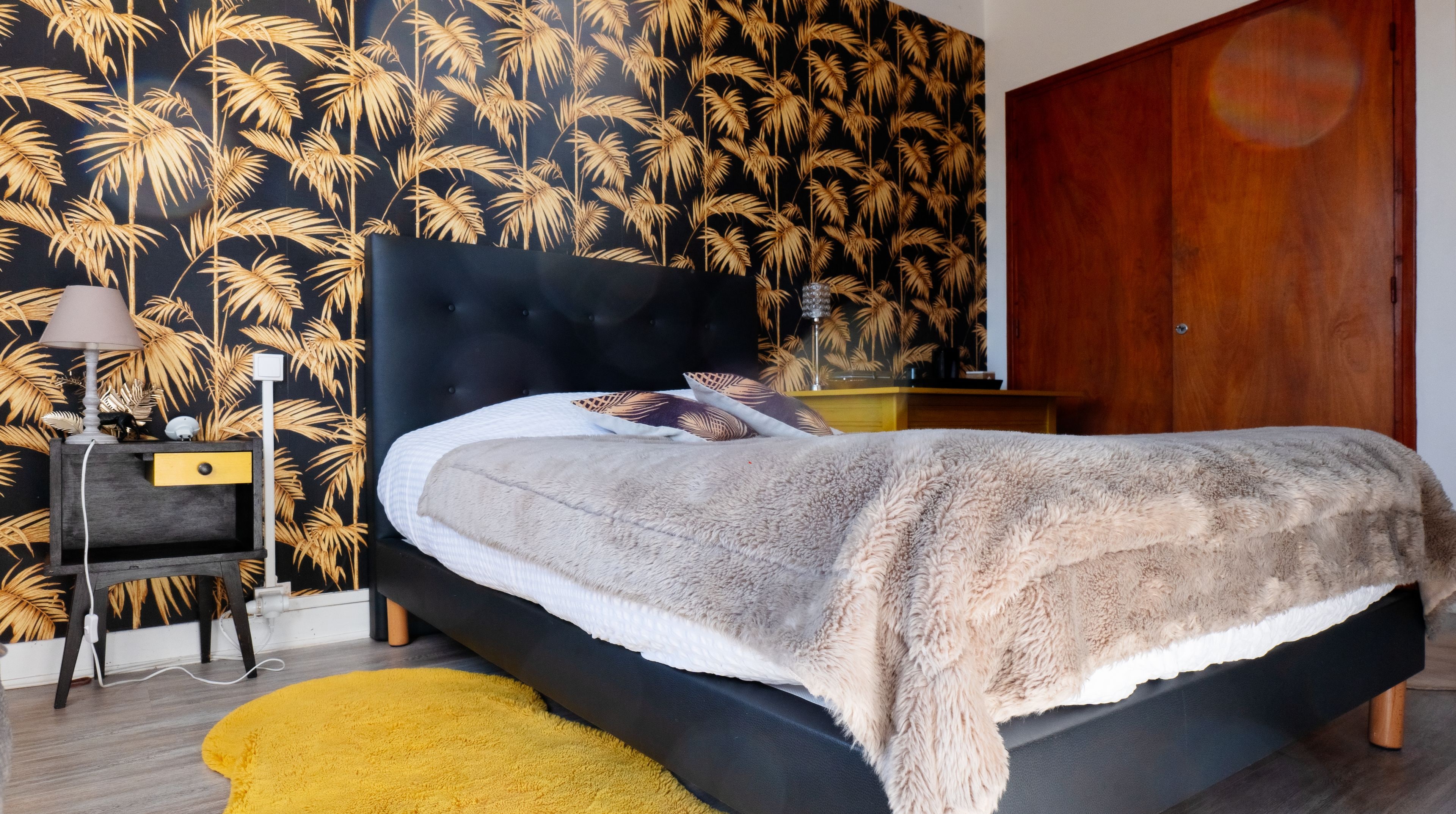 Quarto com uma cama grande, mesa de cabeceira, abajur e guarda-roupa.