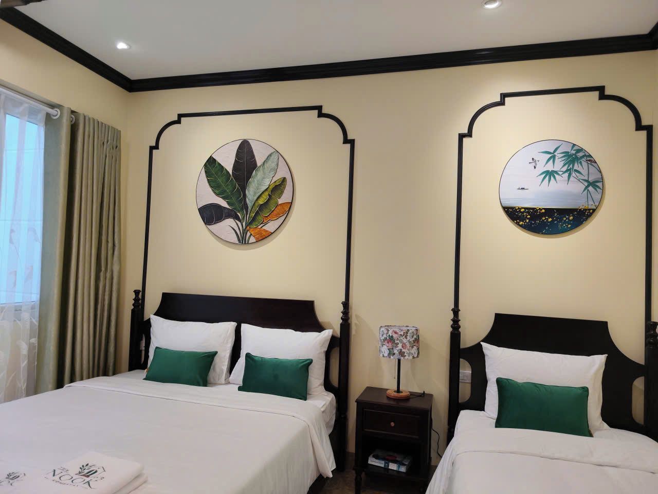 Quarto de hotel com duas camas, cada uma com cabeceira, mesa de cabeceira com abajur e obras de arte nas paredes.