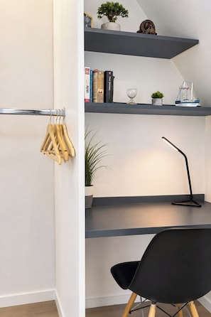 Um interior moderno com uma cadeira preta, uma estante de metal com cabides e uma mesa com abajur.