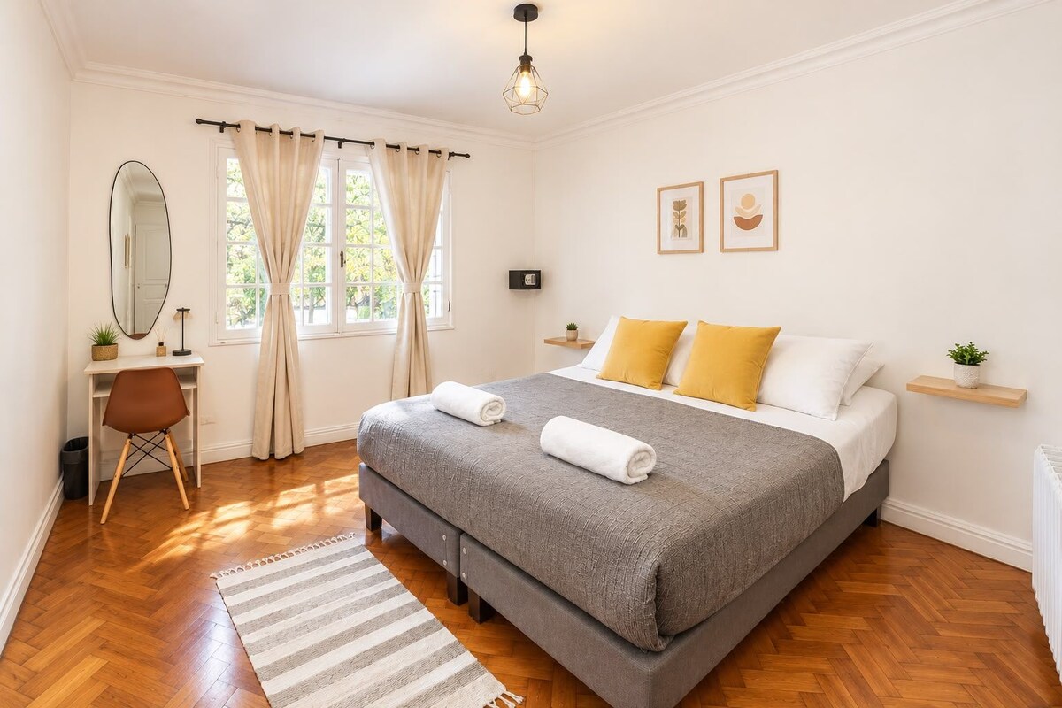 Quarto bem arrumado com uma cama, mesas de cabeceira, escrivaninha e uma cadeira.