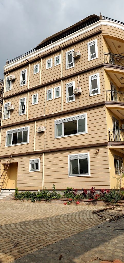 Edifício de vários andares com varandas, aparelhos de ar condicionado e área de entrada pavimentada com plantas.