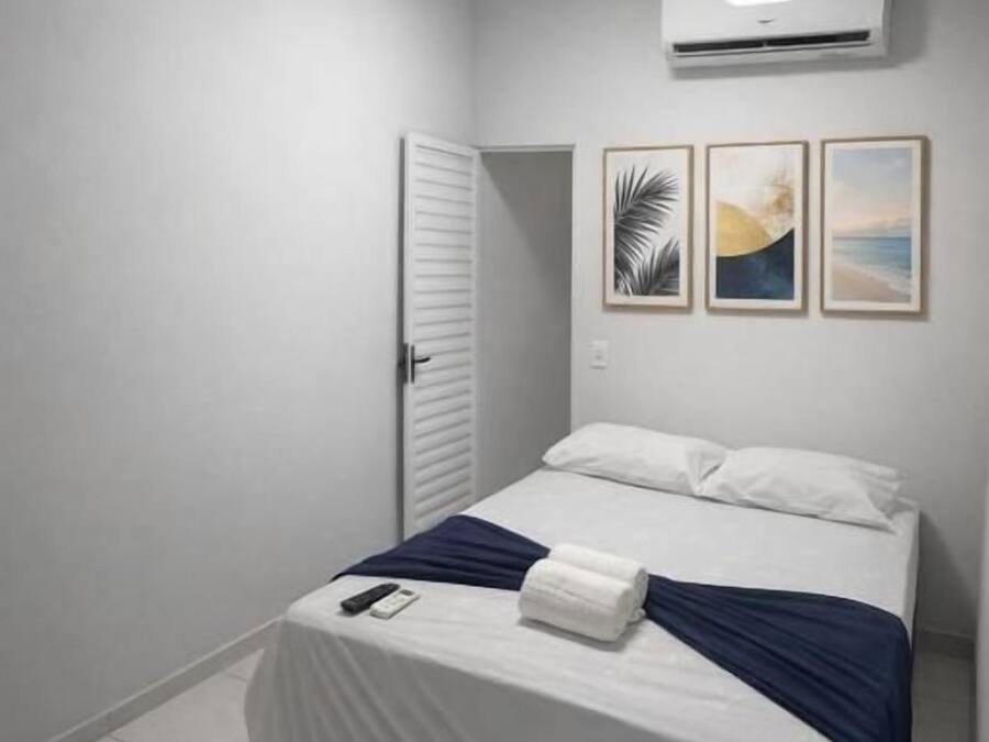 Quarto com cama, paredes brancas, uma porta e ar condicionado.