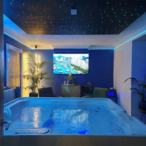 Quarto com uma banheira grande, televisão exibindo uma vista urbana e teto com luzes que lembram estrelas.
