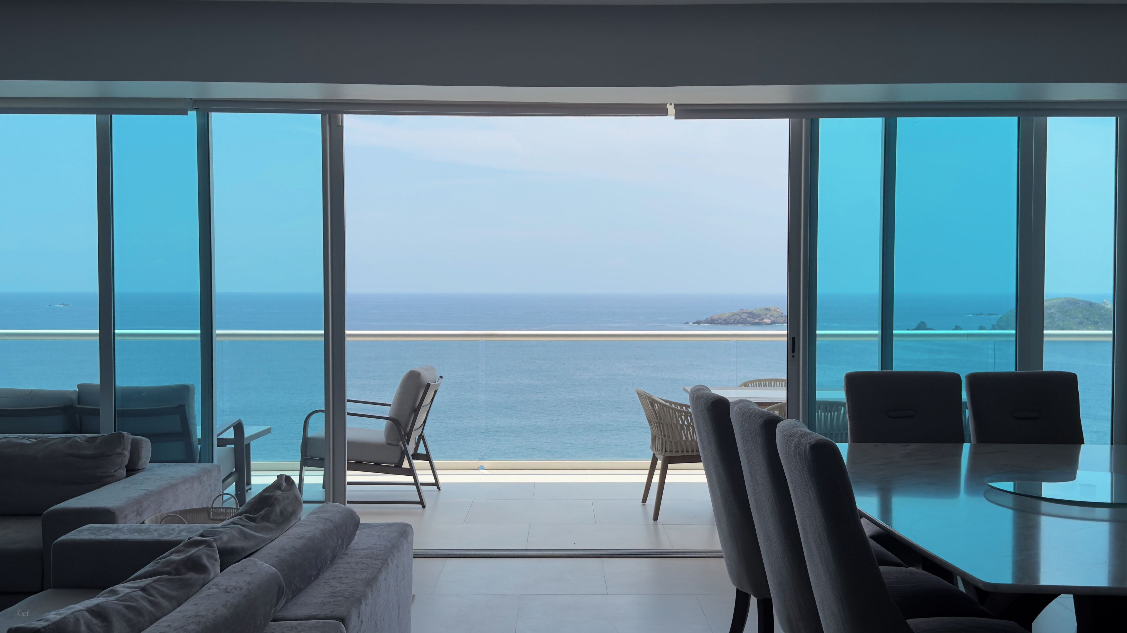 Interior moderno com uma grande porta de vidro que dá para uma varanda com vista para o mar.