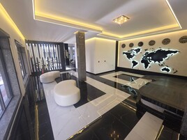 Um lobby moderno com piso quadriculado em preto e branco, área de estar com cadeiras brancas, um mapa decorativo do mundo na parede e um lustre.