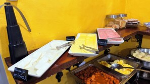 Buffet com diversas opções de comida, incluindo queijos, doces e carnes.