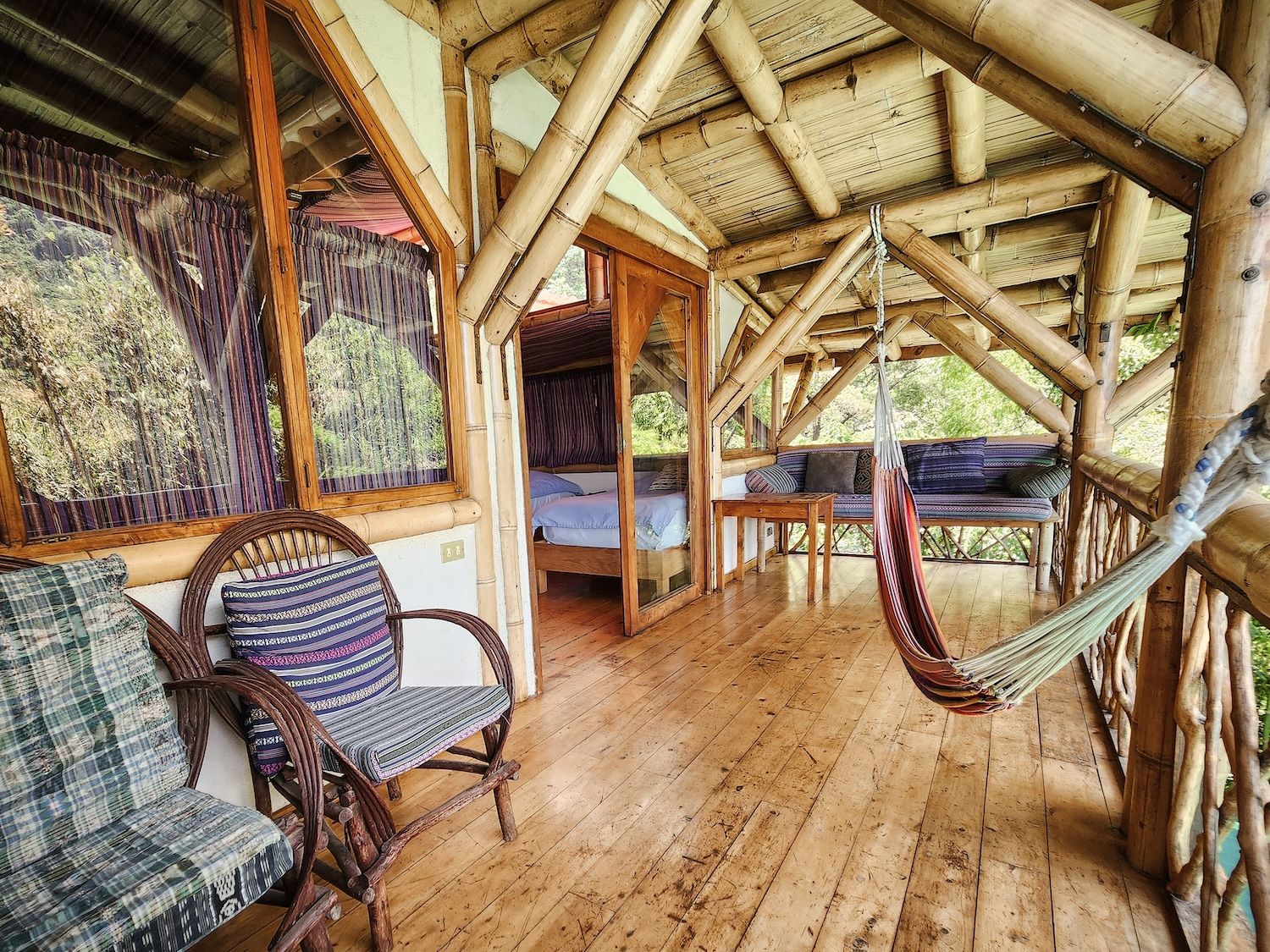 Um deck de madeira com rede, cama e  área de estar com vista para o exterior.