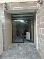 Entrada de um edifício com porta de vidro, parede de pedra e chão de azulejos.