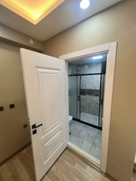 Quarto com porta branca, área de chuveiro com portas de vidro e piso revestido de azulejos.