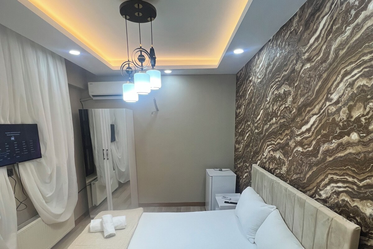 Quarto de hotel moderno com uma cama grande, televisão de tela plana na parede e uma parede decorativa com padrão de mármore.