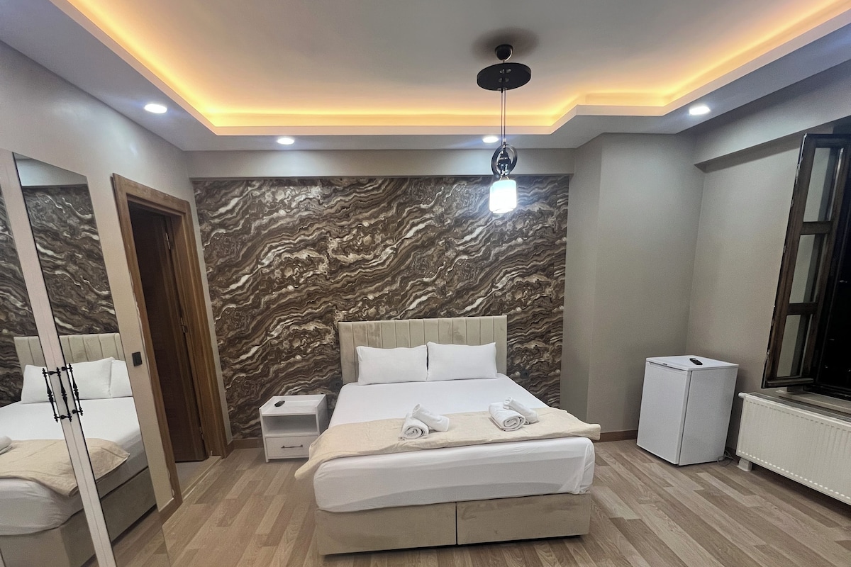 Quarto moderno com uma cama grande, parede com padrão marmorizado e luminária no teto.