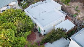 Um edifício de vários andares com telhado plano, cercado por vegetação e um quintal com cerca.