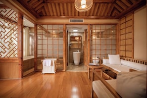 Um quarto tradicional em estilo japonês, com portas deslizantes, piso de madeira, um sofá branco e uma pequena mesa com um livro.