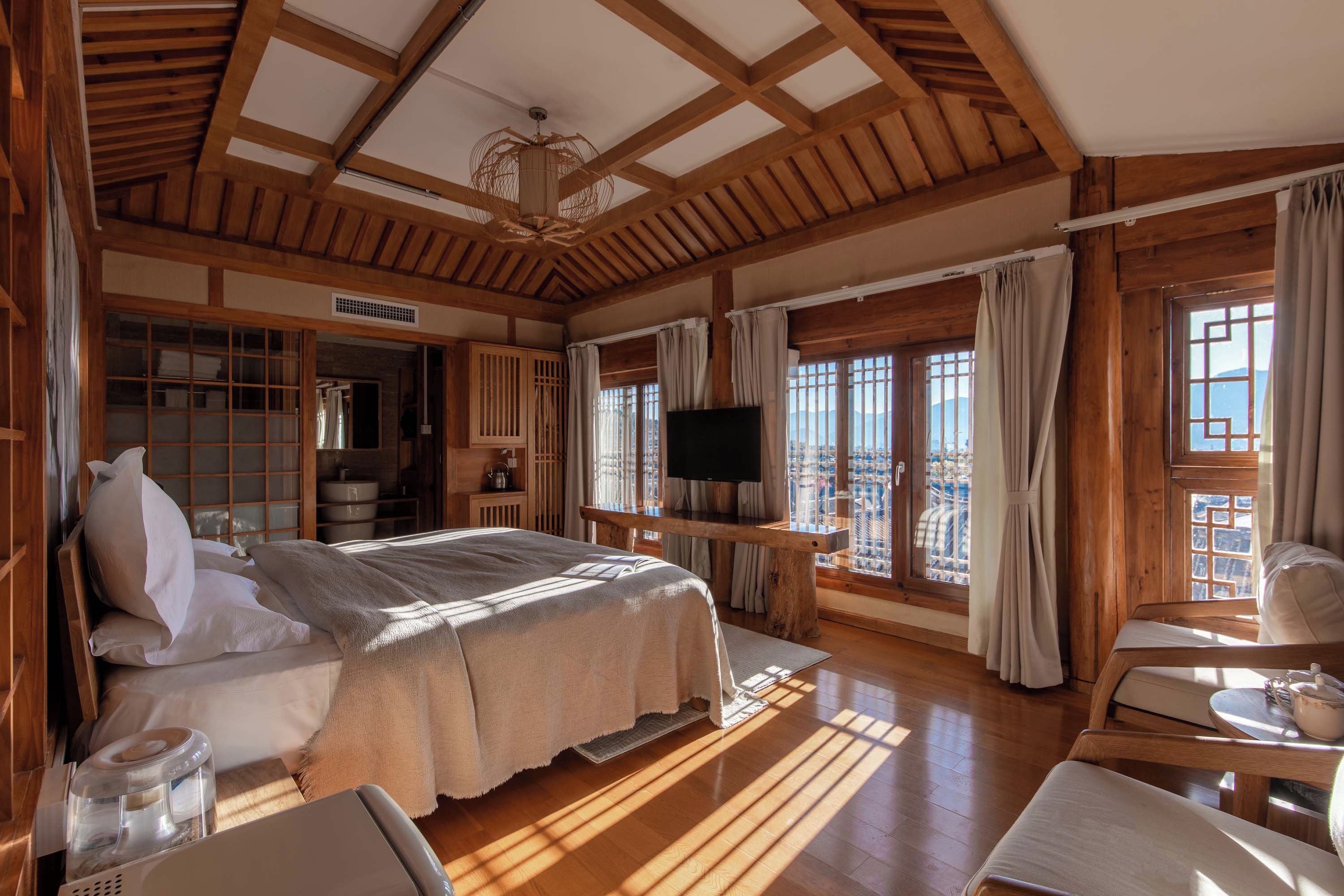 Quarto de madeira tradicional com cama, televisão e vista para o exterior através de janelas amplas.
