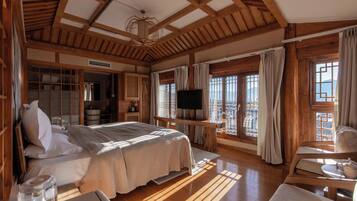 Quarto de madeira tradicional com cama, televisão e vista para o exterior através de janelas amplas.
