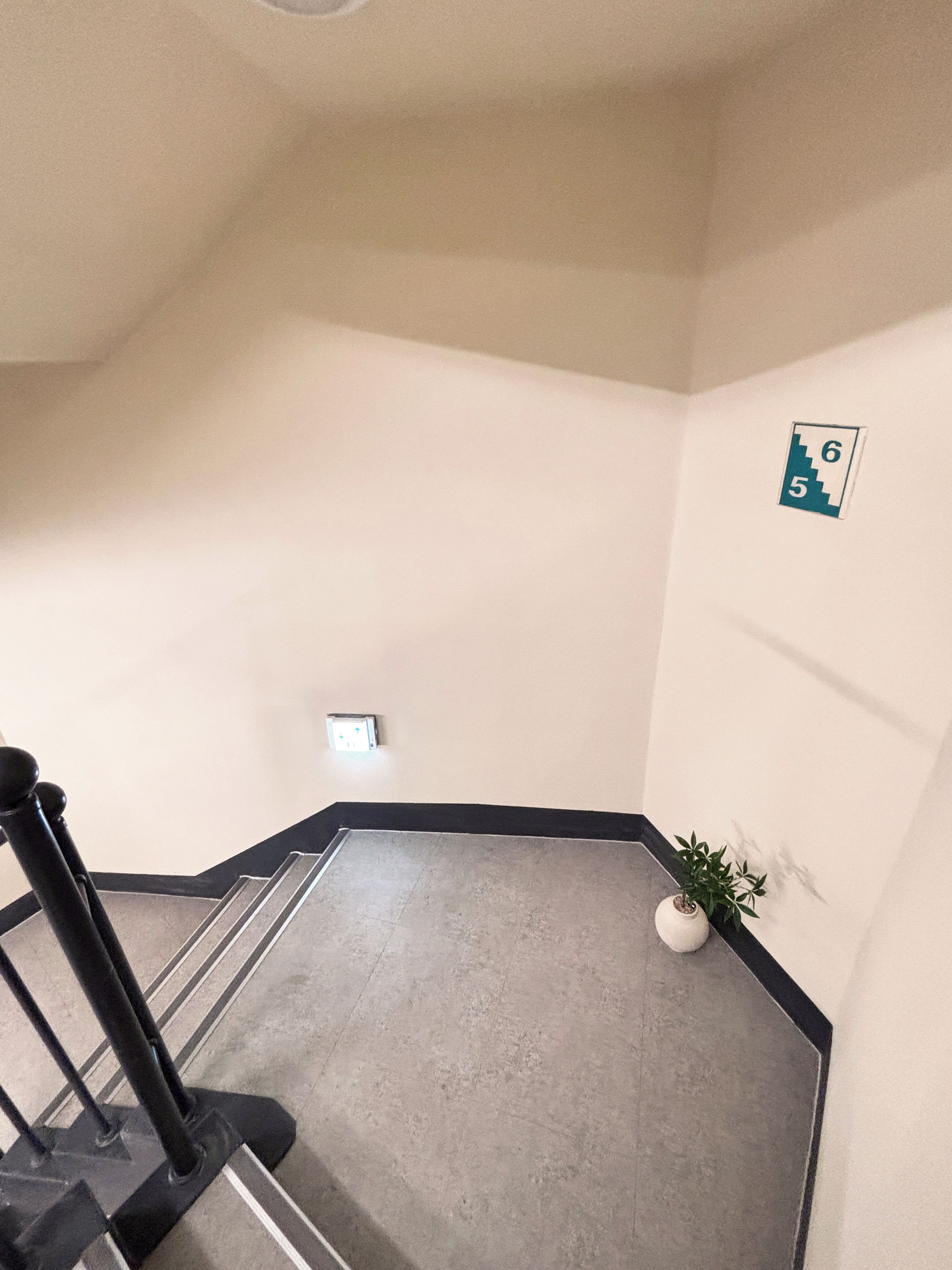 Um corredor com corrimão, um vaso de planta e uma placa na parede indicando números de quartos.