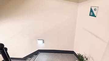 Um corredor com corrimão, um vaso de planta e uma placa na parede indicando números de quartos.
