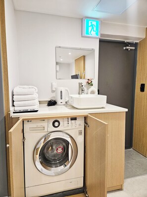 Casa de banho compacta de hotel com máquina de lavar, lavatório e espelho.