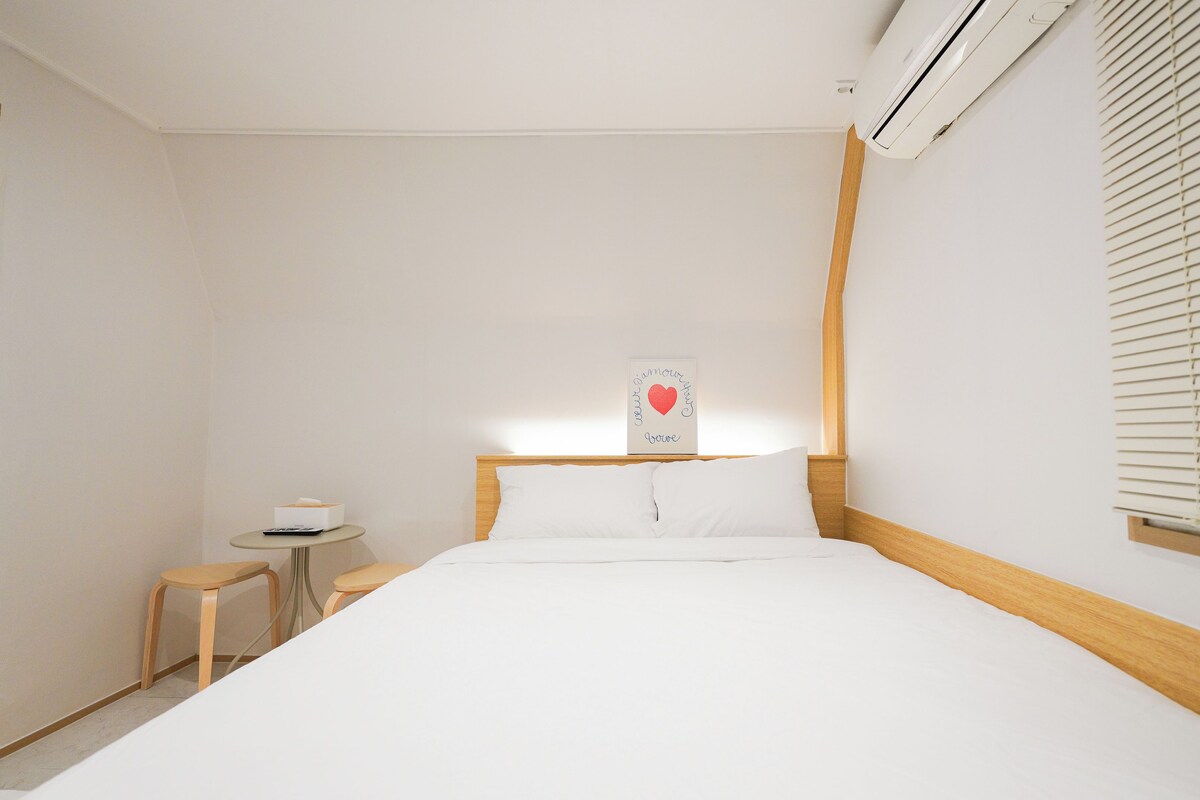 Quarto de hotel com cama, mesa de cabeceira e uma pequena mesa com caixa de lenços.