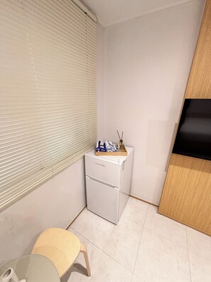 Quarto compacto com geladeira branca, uma mesinha e um armário de madeira.