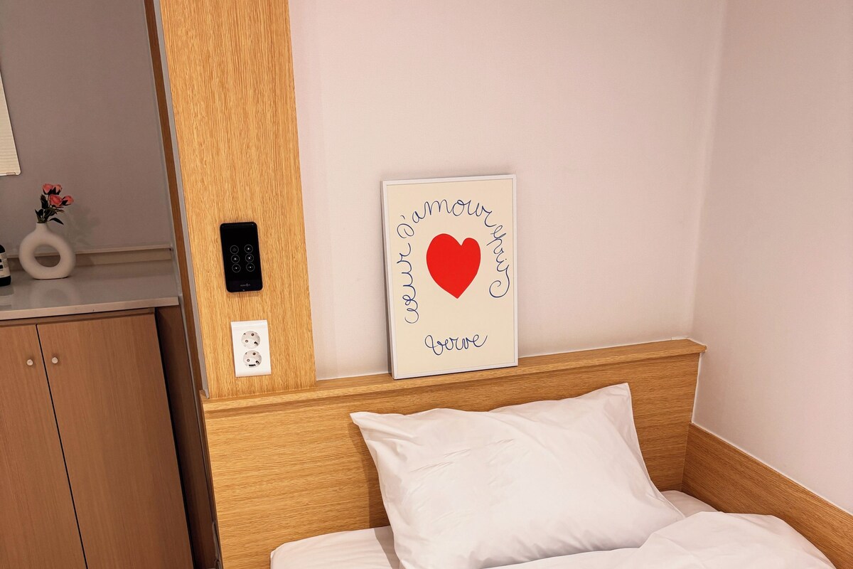 Cama bem arrumada com roupa de cama branca, cabeceira de madeira e painel de controle fixado na parede.