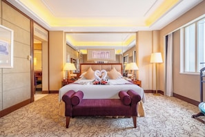 Quarto de hotel com uma cama grande, um banquinho, uma escrivaninha e um espelho.