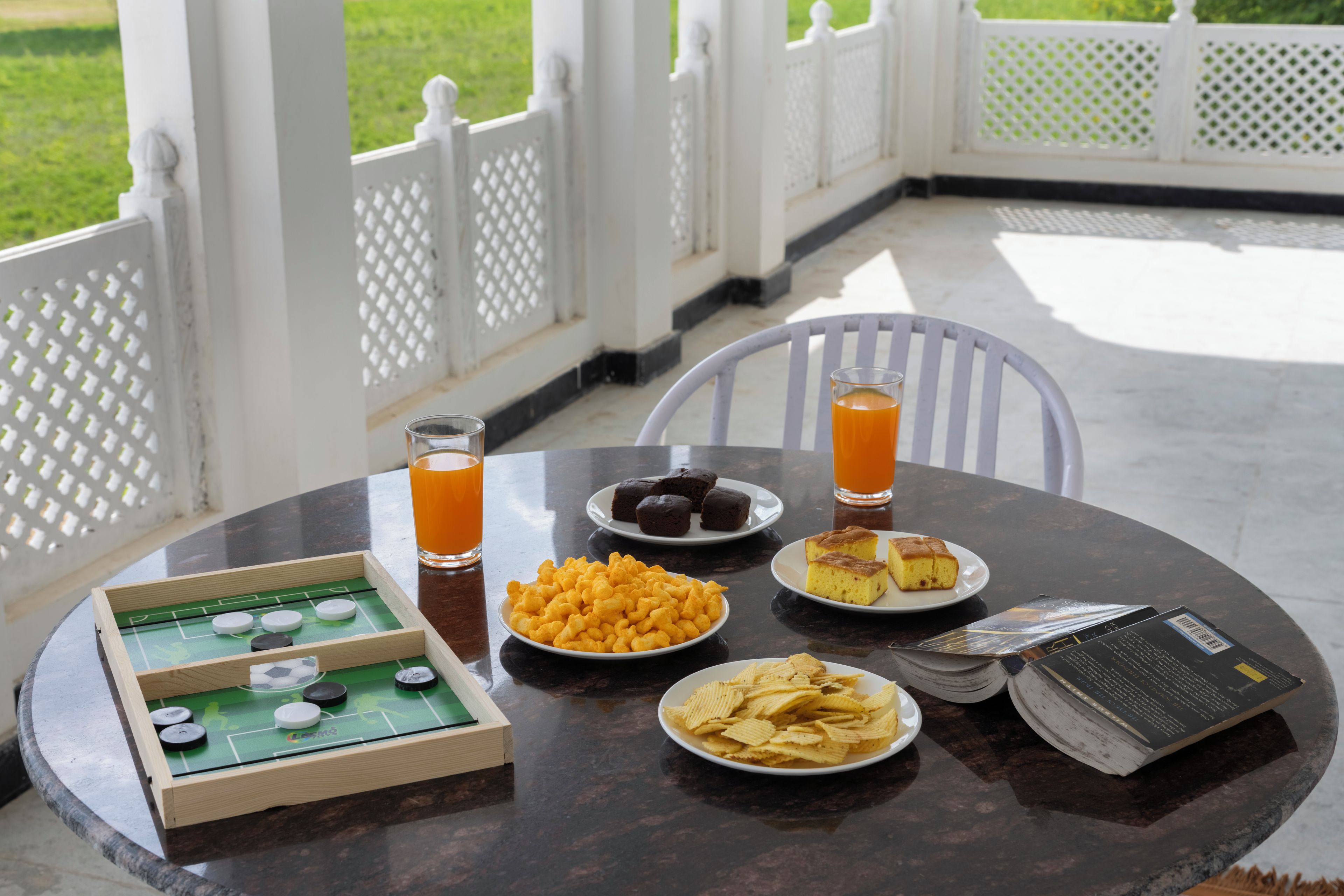 Uma mesa posta com petiscos, bebidas e um jogo de tabuleiro em uma área externa coberta.