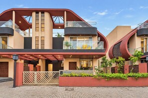 Um edifício moderno de vários andares com design arquitetônico singular, com varandas e entrada protegida por portão.