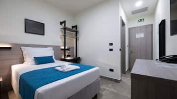 Quarto de hotel com cama, escrivaninha, cadeira, televisão e porta do banheiro.