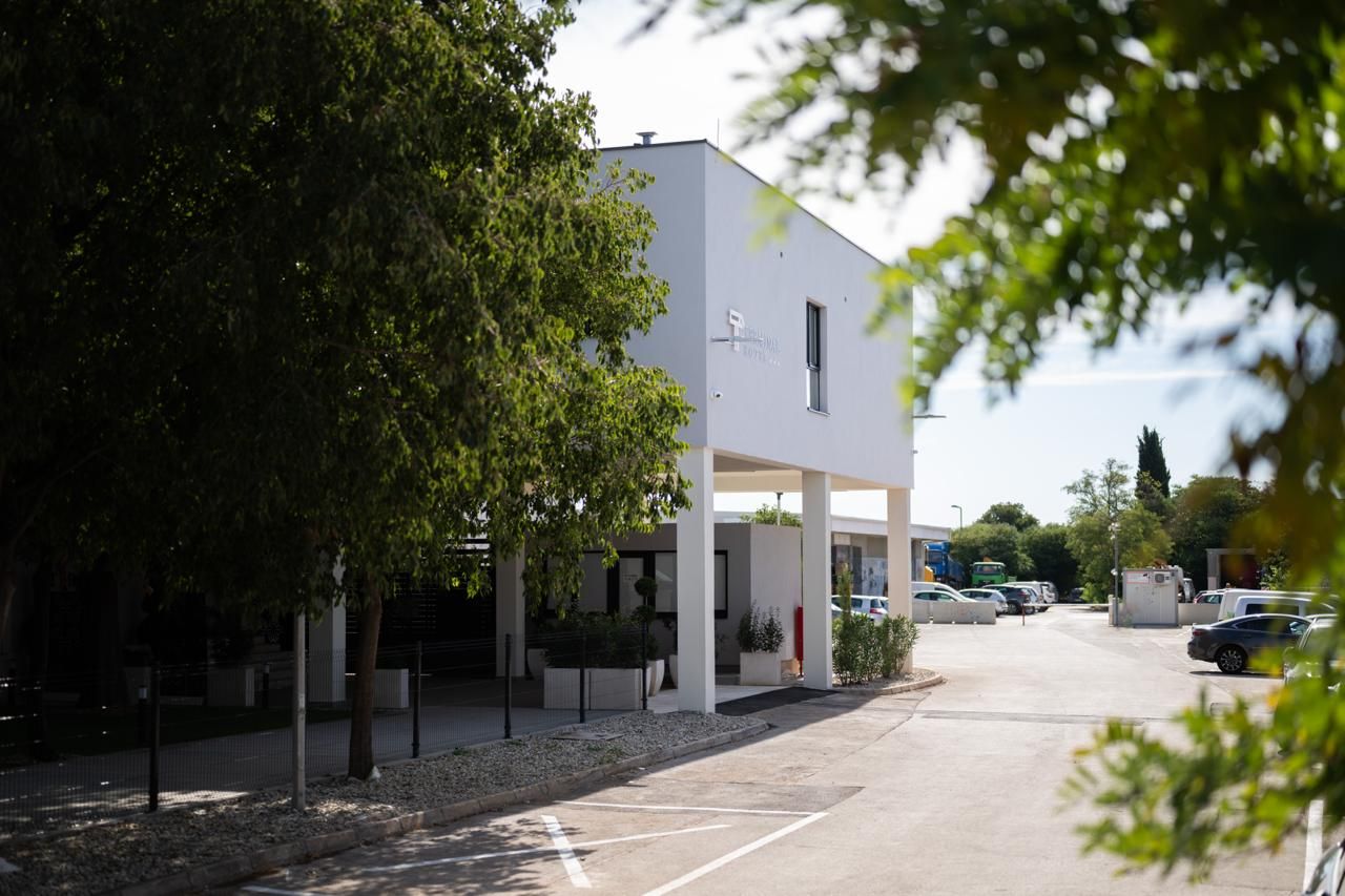 Um edifício moderno com fachada plana, entrada coberta e área de estacionamento com carros.