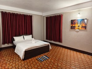 Quarto de hotel com cama, cortinas vermelhas, um quadro na parede e piso estampado.