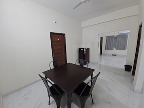 Quarto com porta de madeira, geladeira, mesa de jantar com cadeiras e corredor com piso de azulejos.