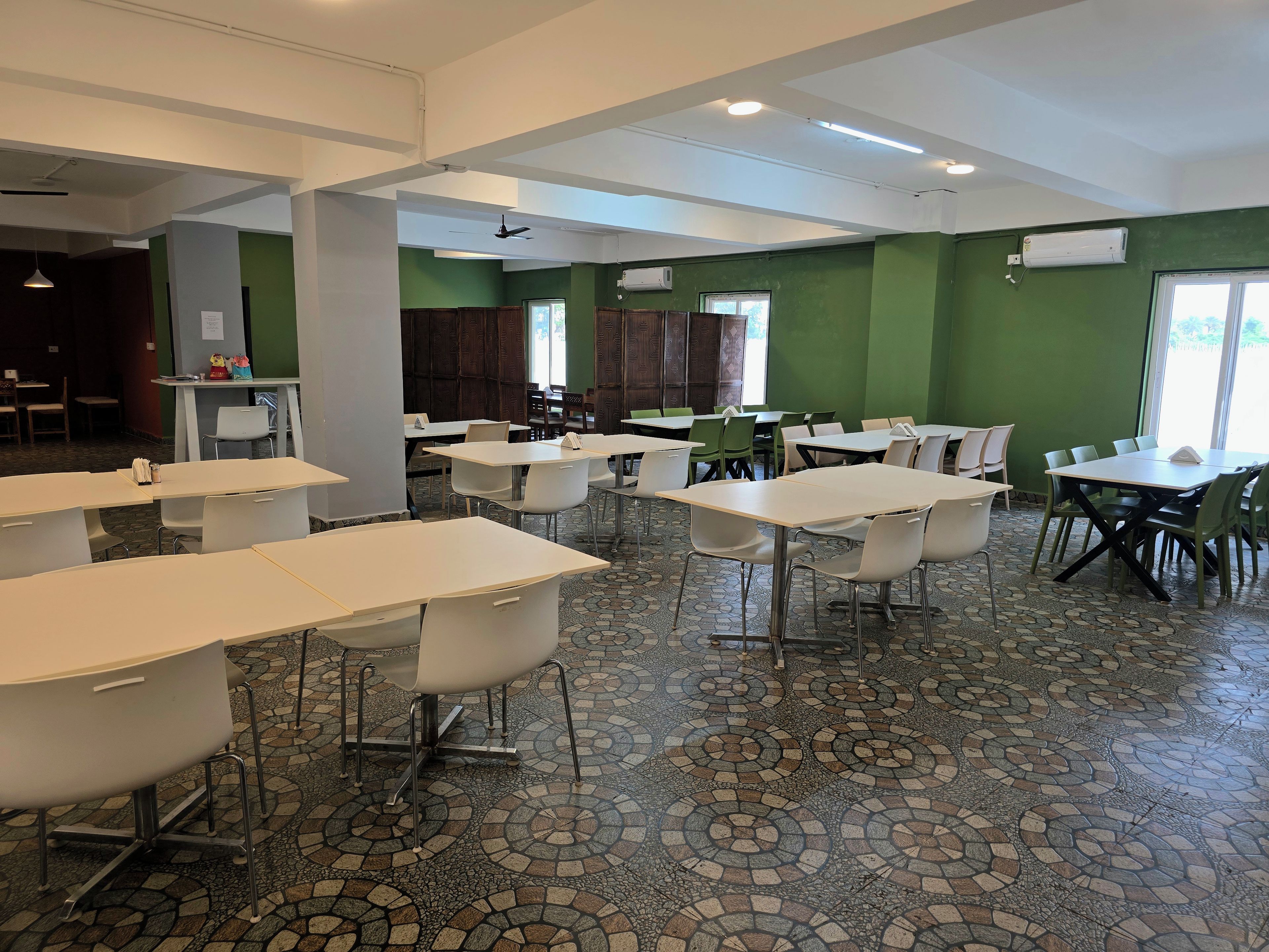 Um espaço amplo e interno com várias mesas e cadeiras, piso estampado e paredes verdes.