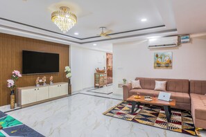 Uma sala de estar moderna com televisão de tela plana, lustre, ventilador de teto e sofá com um laptop.