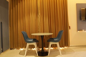 Quarto com cortina, duas cadeiras, uma mesa e um espelho na parede.