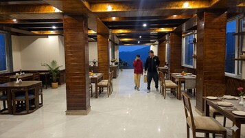 Restaurante com pilares de madeira, mesas, cadeiras e vista para as montanhas.