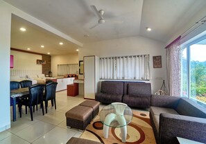 Sala de estar moderna com área de jantar, um sofá, mesa de centro de vidro e vista para o verde lá fora.