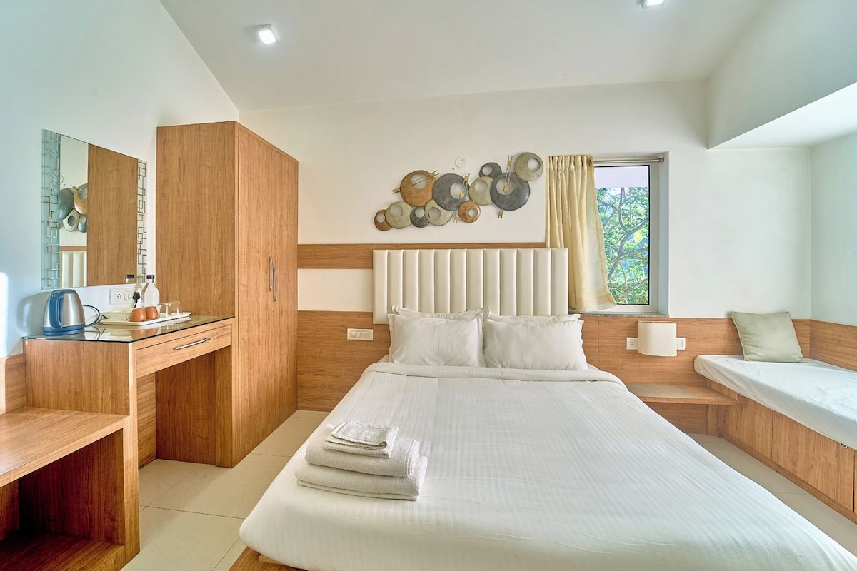 Quarto moderno com uma cama grande, guarda-roupa de madeira, mesa de cabeceira e luminária fixa na parede.