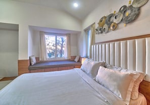 Quarto com cama grande, assento junto à janela e um objeto decorativo na parede.