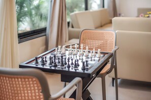 Um tabuleiro de xadrez sobre uma mesa em um quarto com janela, um sofá e uma cadeira.
