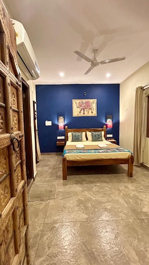 Quarto com cama, ventoinha no teto, ar condicionado fixado na parede e porta com detalhes elaborados.