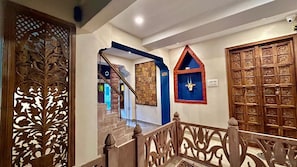 Uma escadaria com corrimão decorativo, uma parede azul de destaque e uma porta de madeira com detalhes entalhados.
