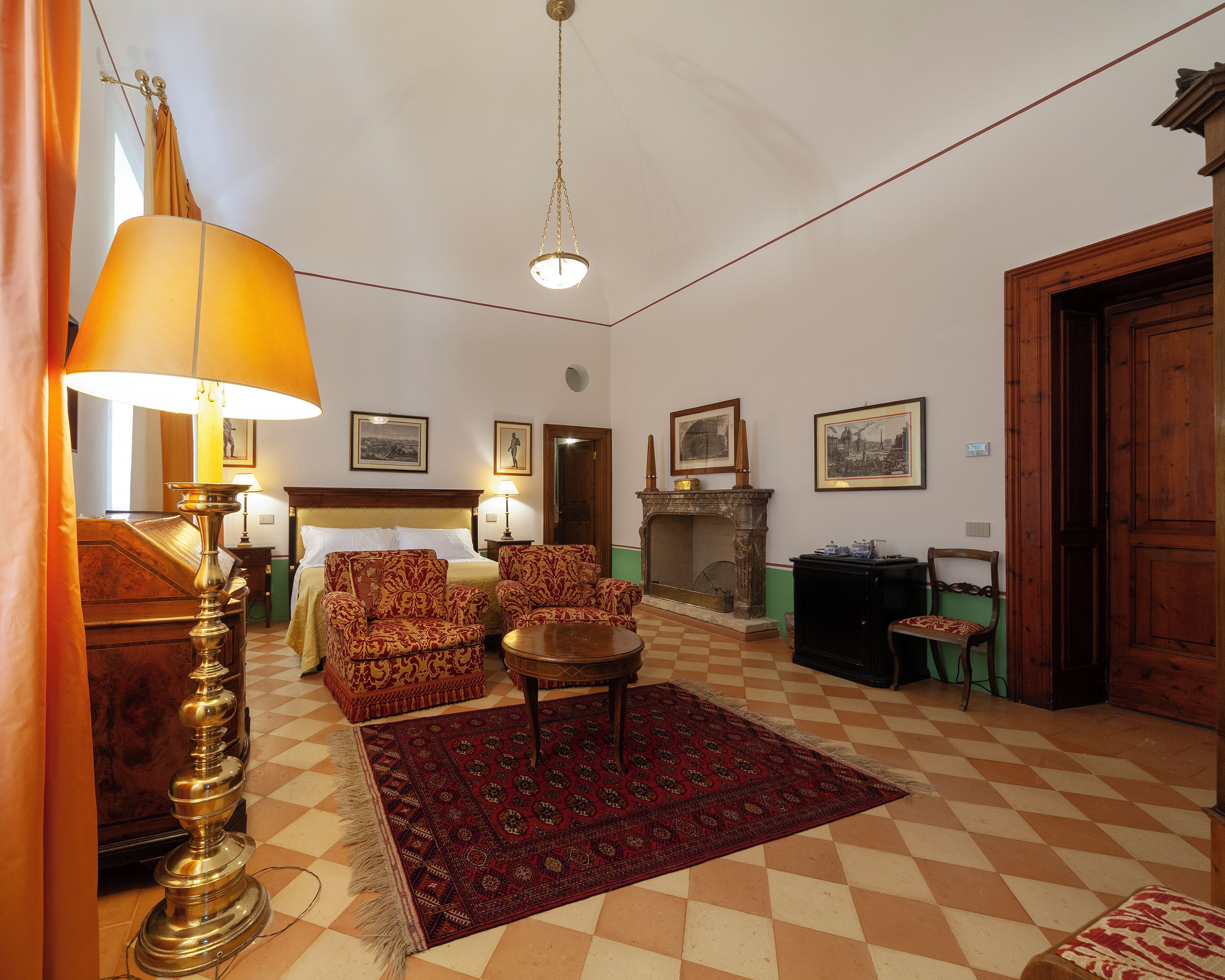 Um quarto com piso xadrez, lareira, dois poltronas, uma mesa e um abajur.