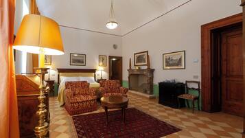 Um quarto com piso xadrez, lareira, dois poltronas, uma mesa e um abajur.