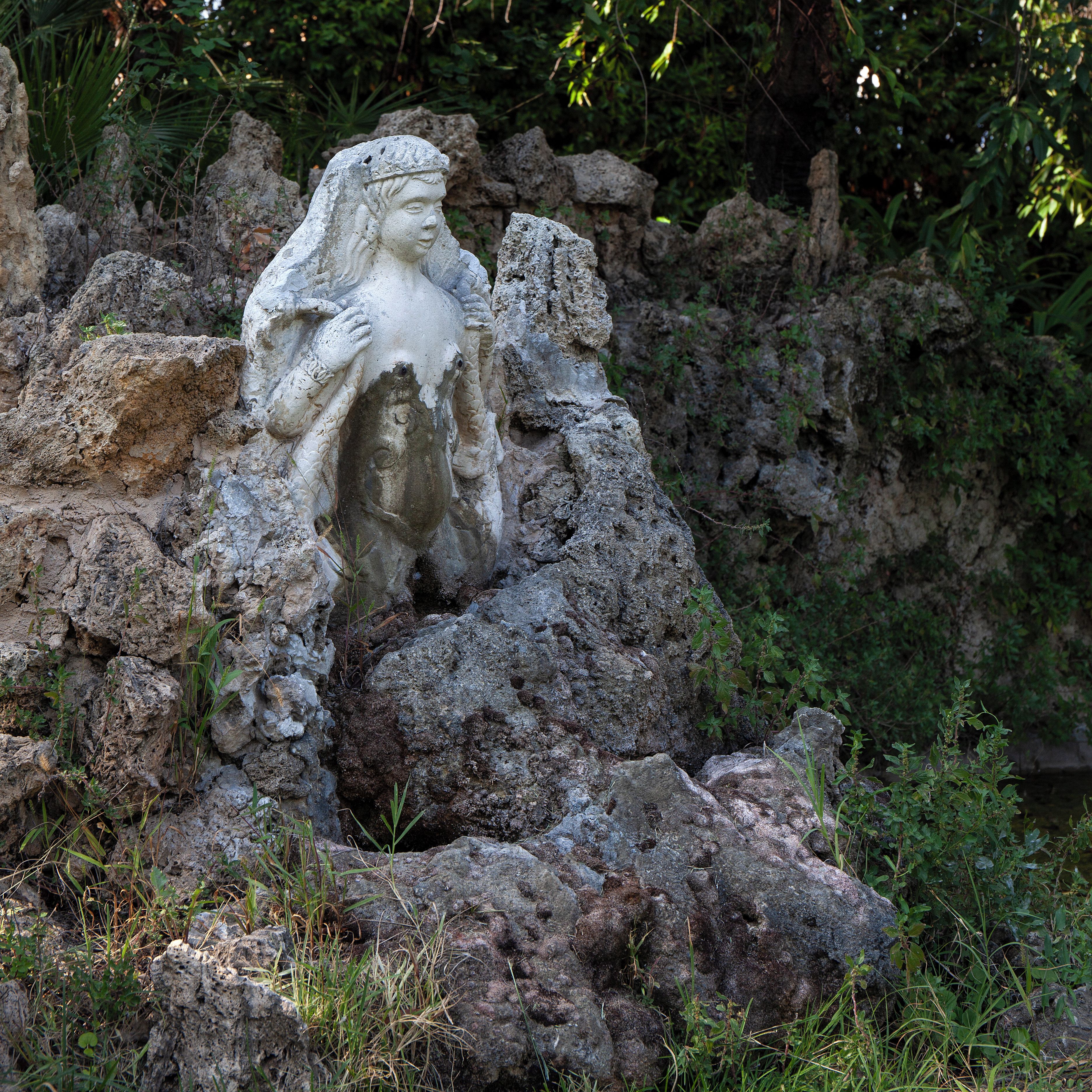 Escultura de pedra parcialmente incrustada em terreno rochoso, com vegetação ao redor.
